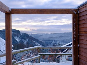 Varanda de madeira com vista para montanhas cobertas de neve e um céu nublado.