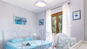 Quarto com cama, uma cadeira, janela com cortinas e duas imagens penduradas na parede.
