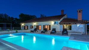 Uma piscina com espreguiçadeiras e uma casa com telhado em azulejo.