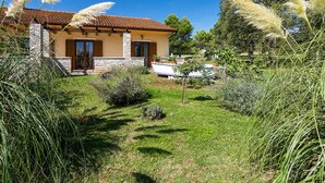 Uma casa com fachada de pedra, telhado telhado e um jardim bem cuidado com grama alta e um pequeno barco ao fundo.