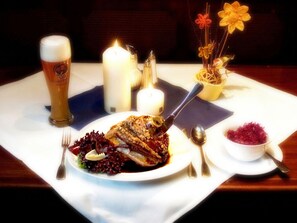 Uma mesa de jantar com um prato de comida, um copo de cerveja, velas e um vaso com flores.