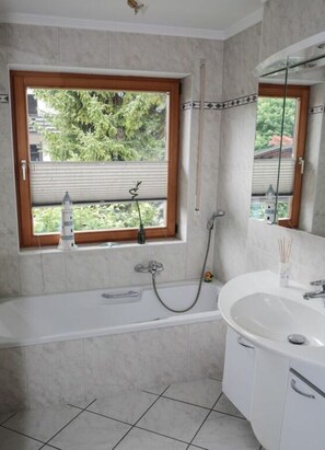 Casa de banho moderna com banheira, lavatório e janela com vista para o verde.