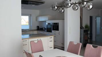 Uma cozinha moderna com armários brancos, uma ilha central e um espaço de jantar com cadeiras cor-de-rosa.
