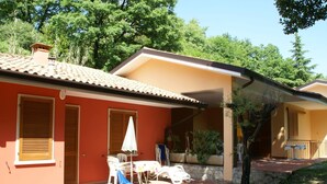 Uma casa de dois andares com fachada vermelha e telhado de telhas. Possui um alpendre com móveis de exterior e uma mesa.
