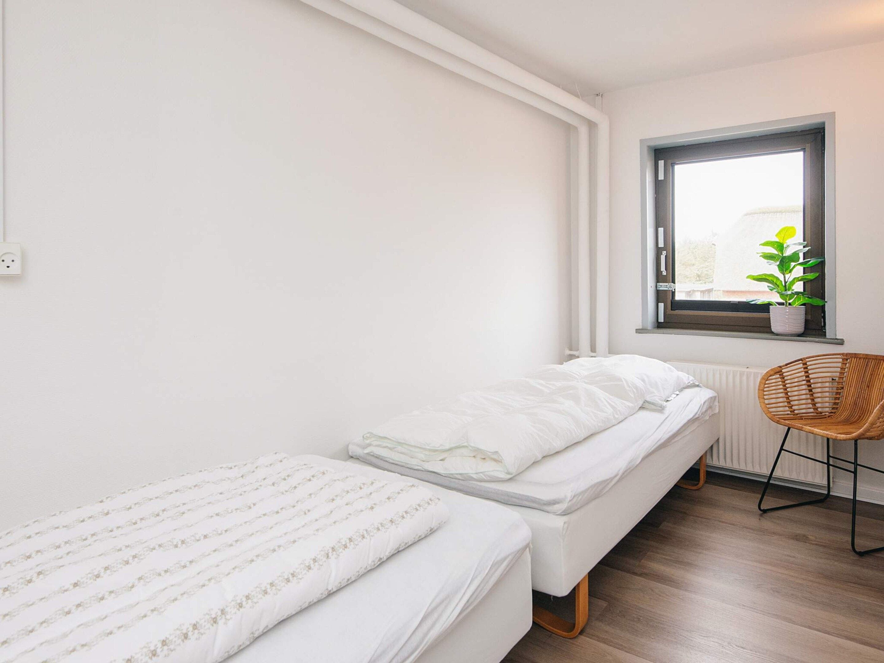Quarto pequeno e limpo com duas camas de solteiro, janela com vista, radiador e uma cadeira.
