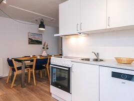 Uma cozinha compacta com armários brancos, fogão, pia e um espaço de refeições com mesa e cadeiras.