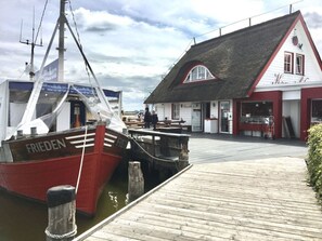 Um cais com um barco vermelho chamado 'FRIEDEN' e um edifício com fachada vermelha e branca.