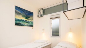 Quarto com duas camas de solteiro, um quadro de um mar agitado, janela com vista e um ventilador de teto.
