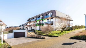 Um edifício residencial moderno com vários andares, varandas, garagem e área de jardim ajardinada.