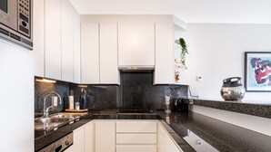 Cozinha moderna com armários brancos, bancada preta e eletrodomésticos de aço inoxidável.