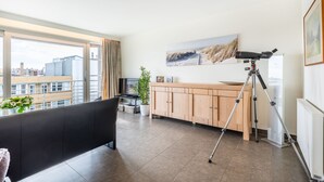 Uma sala de estar moderna com uma janela grande, um sofá preto, um armário de madeira e um telescópio sobre um tripé.