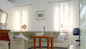 Uma sala de estar com piso xadrez, dois sofás, uma pequena mesa de madeira, um espelho, um abajur, uma televisão e um quadro na parede.