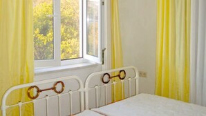 Quarto com uma cama de solteiro, janela com cortinas e vista para árvores lá fora.