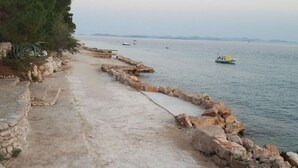 Um caminho costeiro com degraus de pedra que descem até o mar, ladeado por rochas e vegetação rasteira.