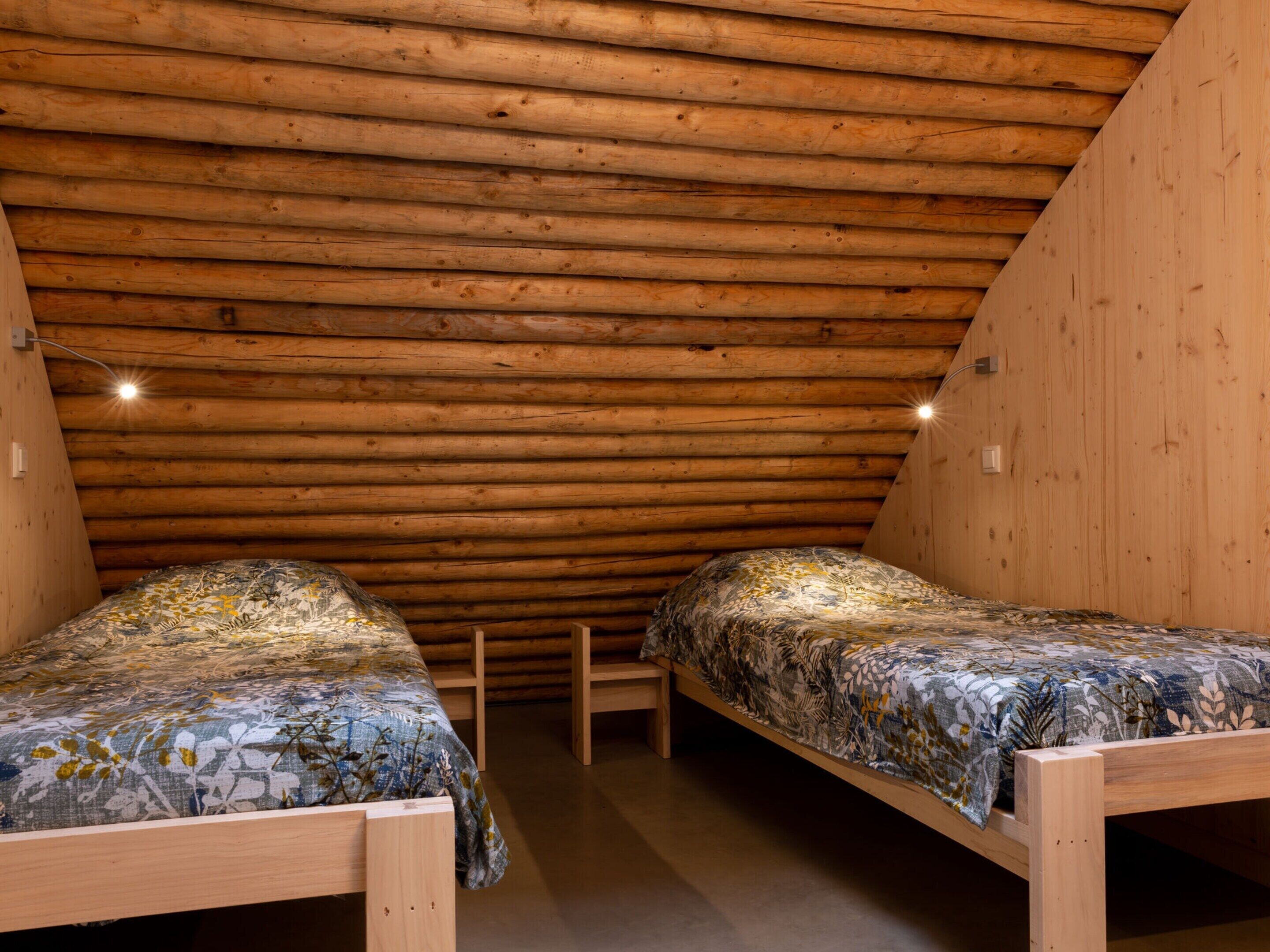Um quarto de sótão aconchegante com duas beliches de madeira, teto inclinado e decoração rústica e simples.