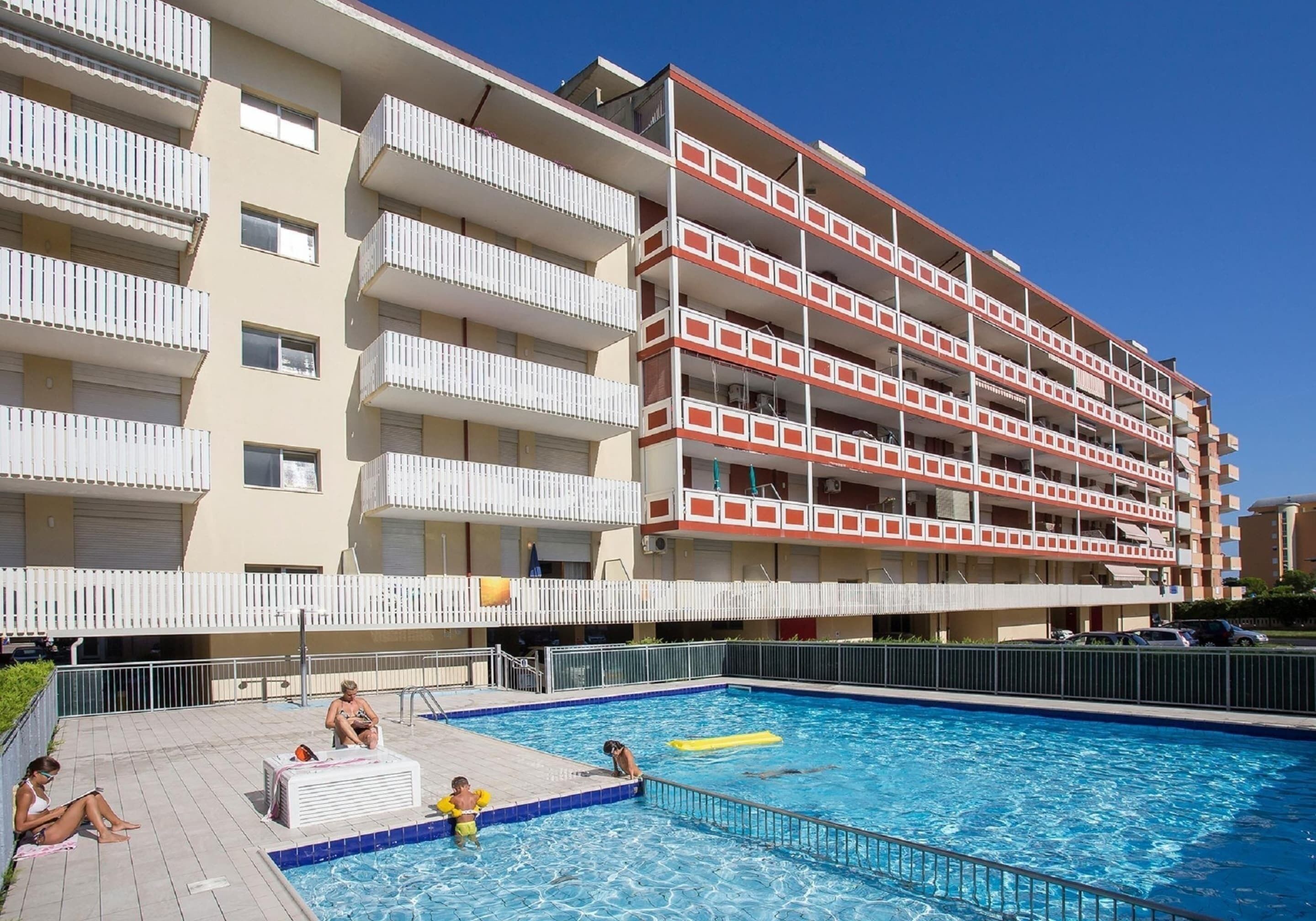 Um hotel com vários andares, varandas, piscina e área de estar coberta.