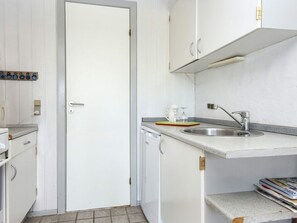 Uma cozinha compacta com armários brancos, uma pia de aço inoxidável e uma bancada pequena.
