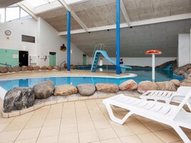 Piscina interna com tobogã, cadeiras de descanso e posto de salva-vidas.