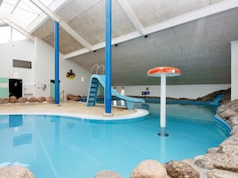 Piscina interna com um escorregador azul, uma cadeira de salva-vidas e borda da piscina revestida com pedras.