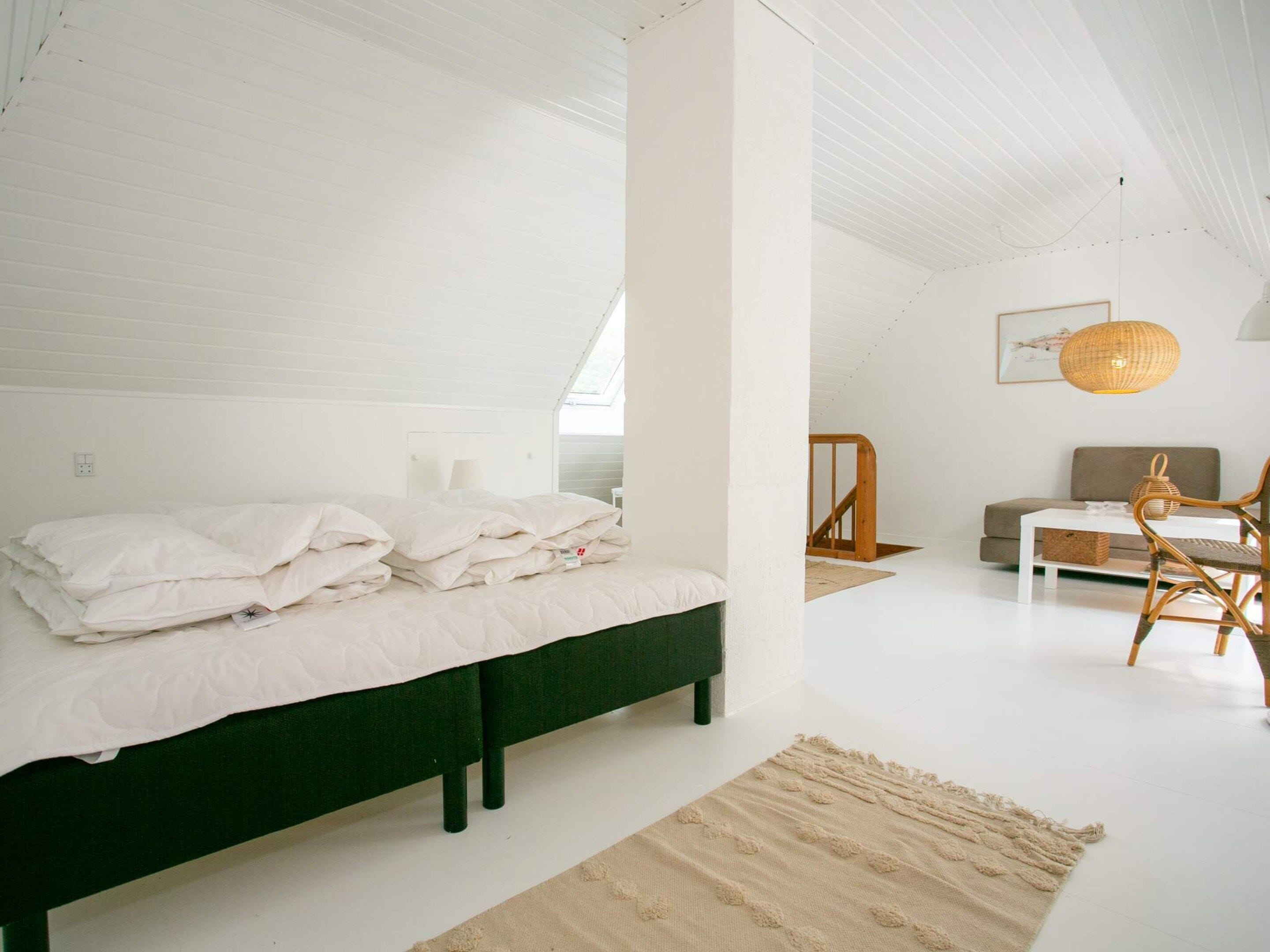 Quarto com cama, sofá, cadeira, mesa e luminária pendente.