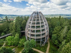 Uma grande estrutura esférica com vários níveis, rodeada por uma floresta densa, com uma ponte que a conduz.