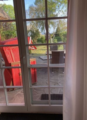 Visão através de uma porta de vidro de um espaço de pátio com mobiliário externo e uma estrutura vermelha.