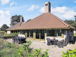 Uma casa com telhado de telhas, chaminé e um alpendre coberto com mobiliário de exterior.