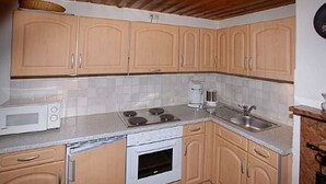 Uma cozinha com armários de madeira, micro-ondas, fogão, cafeteira e pia.
