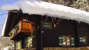 Um chalé de madeira com telhado coberto de neve, uma varanda com grades de madeira e uma placa com a inscrição "Haus zum Grunnt".
