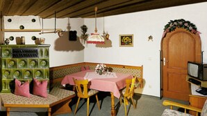 Uma sala de jantar com uma mesa posta para quatro pessoas, um banco de madeira e uma televisão sobre um suporte.