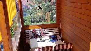 Uma cabana aconchegante com interior de madeira, uma mesa com cadeiras e vista para pássaros voando lá fora.