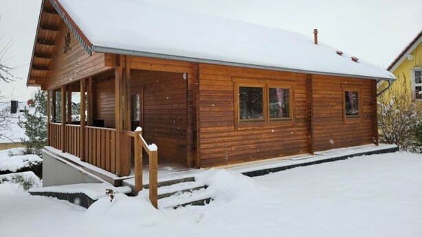 Uma cabana de madeira com varanda e telhado coberto de neve.