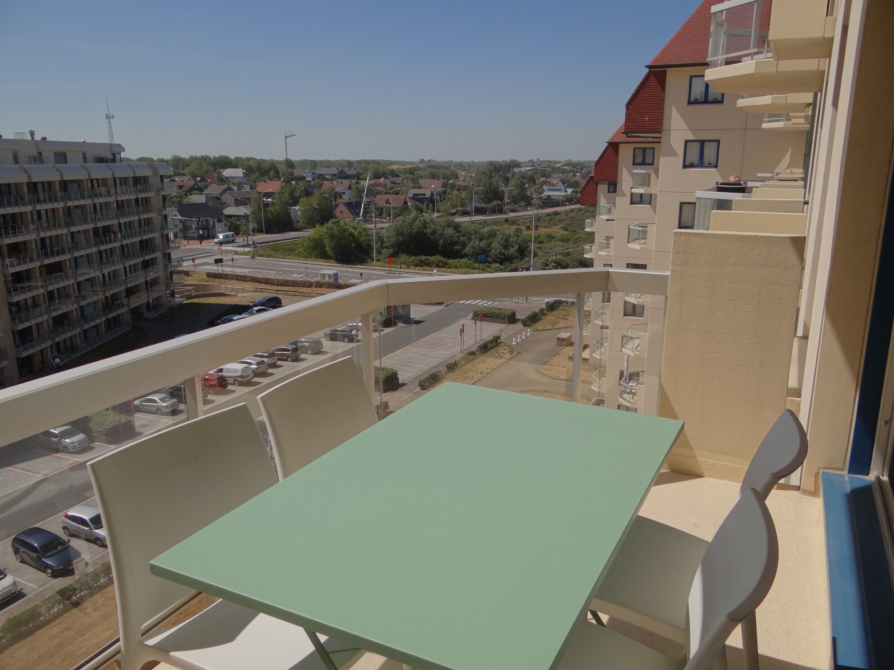 Varanda com mesa e cadeiras, vista para um estacionamento e prédios.