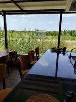 Uma sala de jantar com uma mesa comprida e cadeiras, um dispensador de água e vista para uma estrada e vegetação.