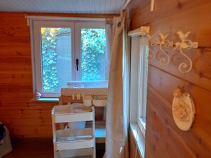 Interior de uma cabana de madeira com uma janela, uma prateleira branca com recipientes e um enfeite de parede decorativo.