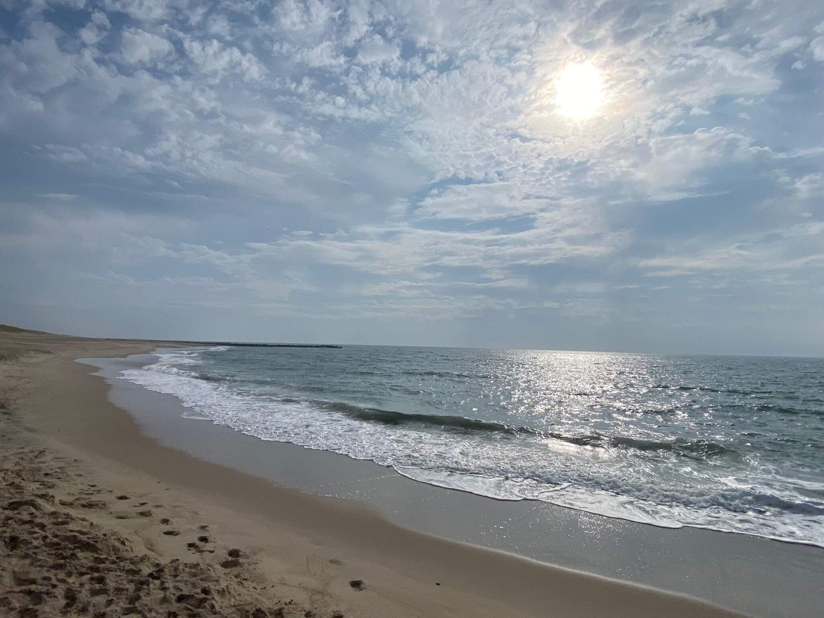 Uma praia com céu claro e luz do sol refletindo na água.