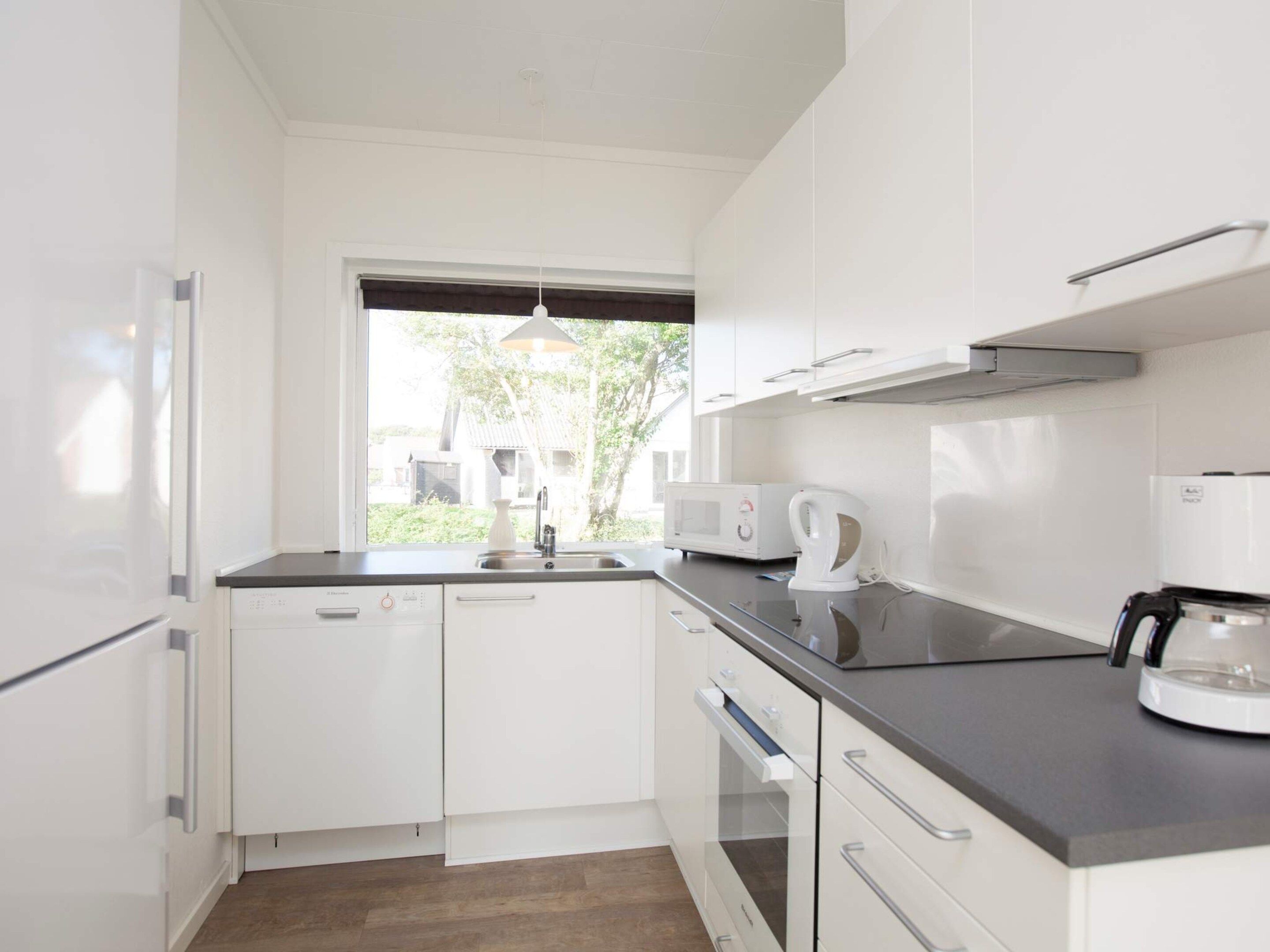 Uma cozinha moderna com armários brancos, bancada preta, forno embutido e uma janela com vista para o verde lá fora.