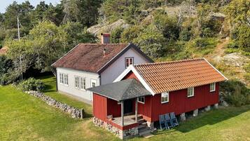 Uma casa de dois andares com fachada vermelha e branca, base de pedra e um gramado.