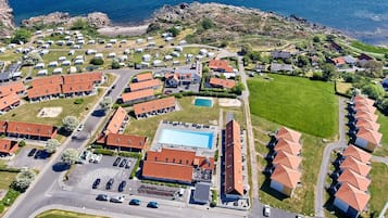 Vista aérea de uma área residencial costeira com vagas para trailers, uma piscina e casas com telhados vermelhos.