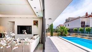 Sala moderna com TV, sofá e plantas de orquídeas. Oferece vista para uma piscina e área residencial.