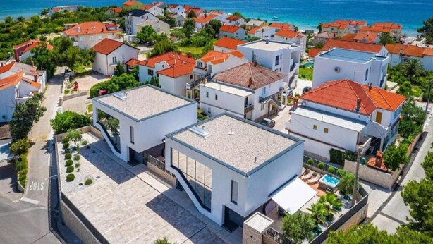 Uma área residencial costeira com casas modernas, mar azul cristalino e uma ilha ao longe.