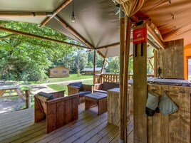 Um deck de madeira com área de estar externa, uma mesa e uma estrutura coberta.