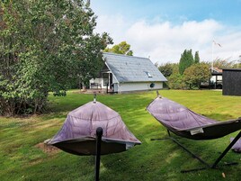 Quintal gramado com duas redes de descanso ao ar livre e uma casa com telhado inclinado.
