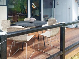 Um terraço com mesa redonda e cadeiras de vime, piso de madeira e corrimão.
