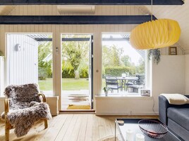 Um quarto com piso de madeira, uma poltrona de pele, um sofá, uma mesa de jantar com cadeiras e um abajur de papel amarelo.