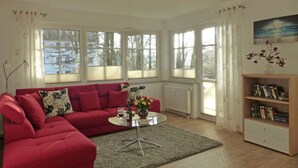 Uma sala de estar com um sofá vermelho, uma mesa de centro redonda e uma estante.