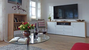 Uma sala de estar moderna com uma mesa de centro de vidro, estante, TV de tela plana e uma janela grande.