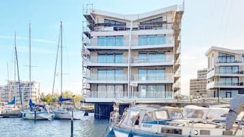 Um edifício com vários andares e varandas, uma marina com barcos, e um céu claro.