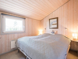 Quarto com cama, janela, quadro fixado na parede e mesa de cabeceira com abajur.
