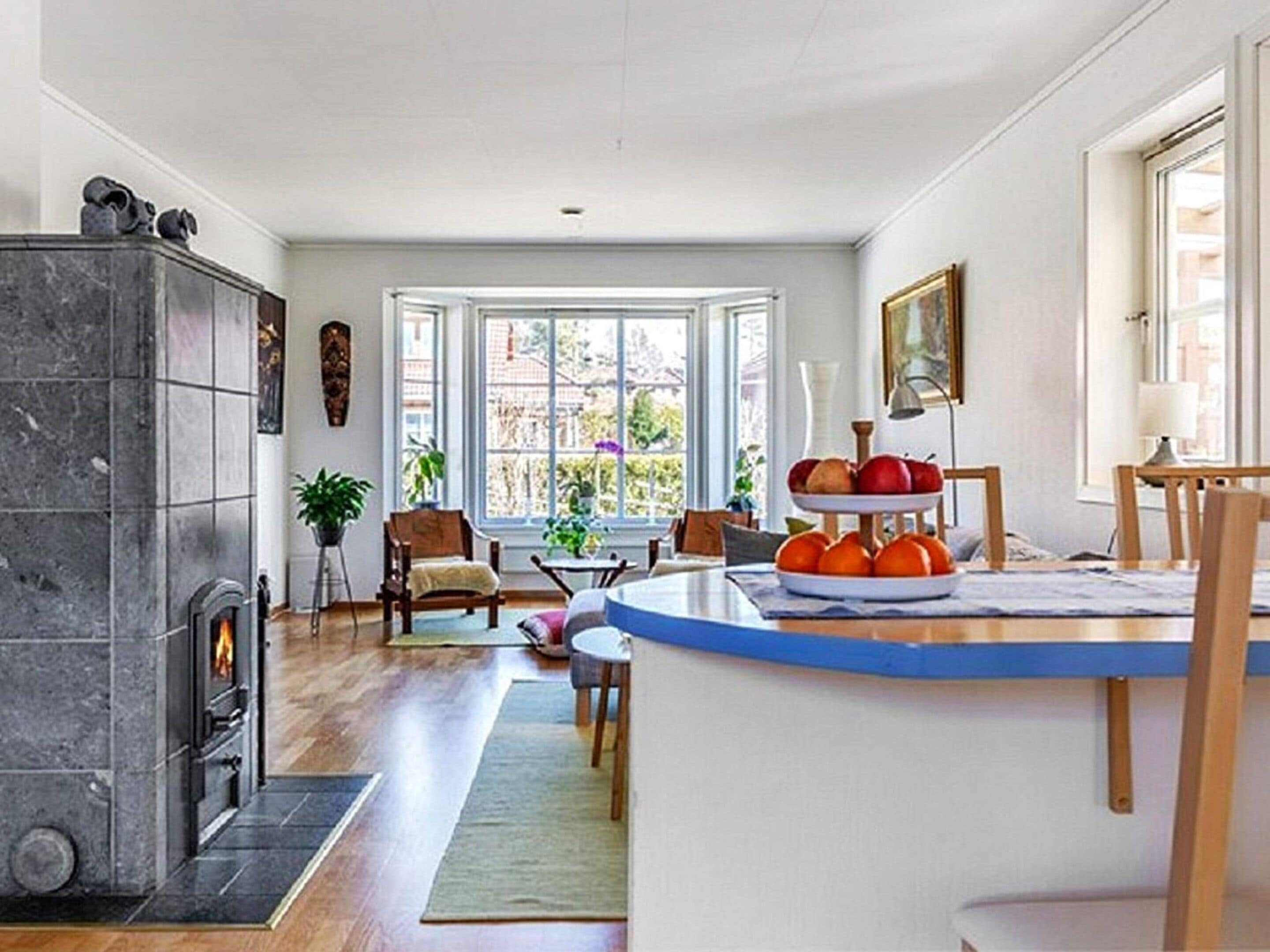 Uma sala de estar moderna com lareira, um espaço de jantar com uma seleção de frutas e grandes janelas com vista para o exterior.